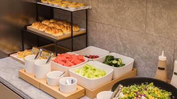 Uma mesa de buffet com diversos alimentos, incluindo pães, frutas e saladas.