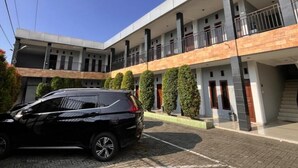 Hotel de vários andares com design moderno, apresentando uma área de estacionamento com um SUV preto.