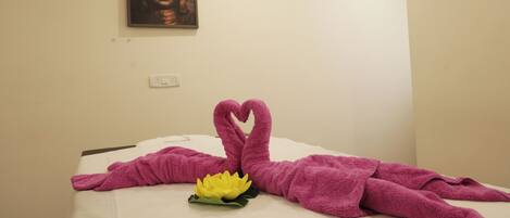 Uma cama com toalhas cor-de-rosa dispostas em formato de coração e uma flor de lótus amarela.
