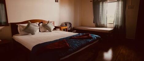 Quarto com cama, almofadas, mesa de cabeceira, cadeira e janela com cortinas.