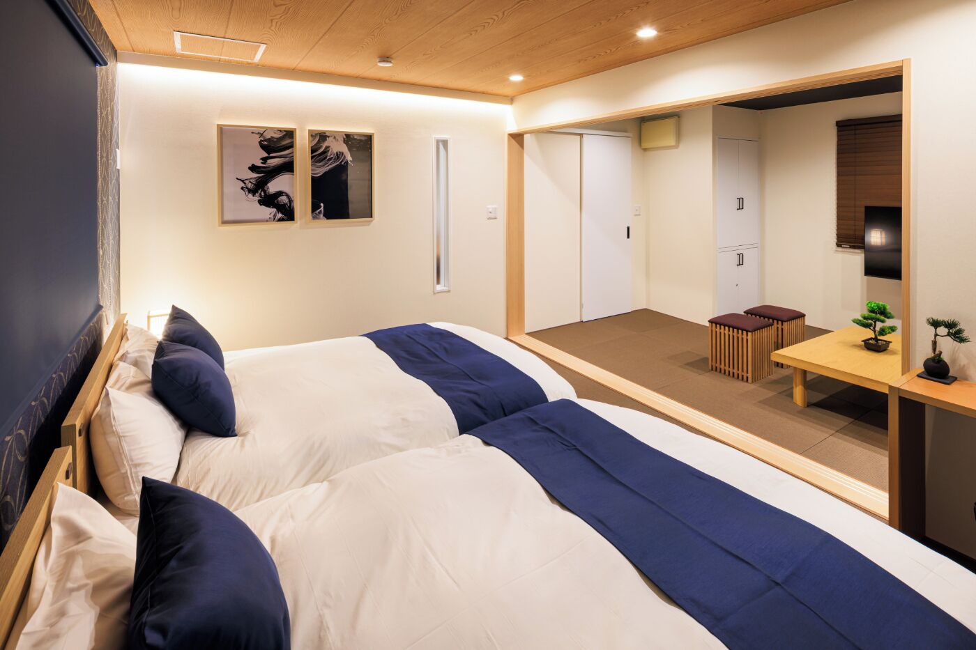 Quarto de hotel moderno com duas camas, uma mesinha com uma planta e um espelho.
