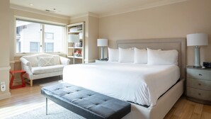 Quarto com cama grande, luminárias laterais, um banco, uma janela e armários embutidos.