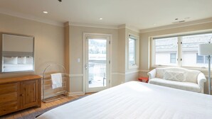 Quarto com cama grande, cómoda de madeira, espelho, janela e porta para varanda.