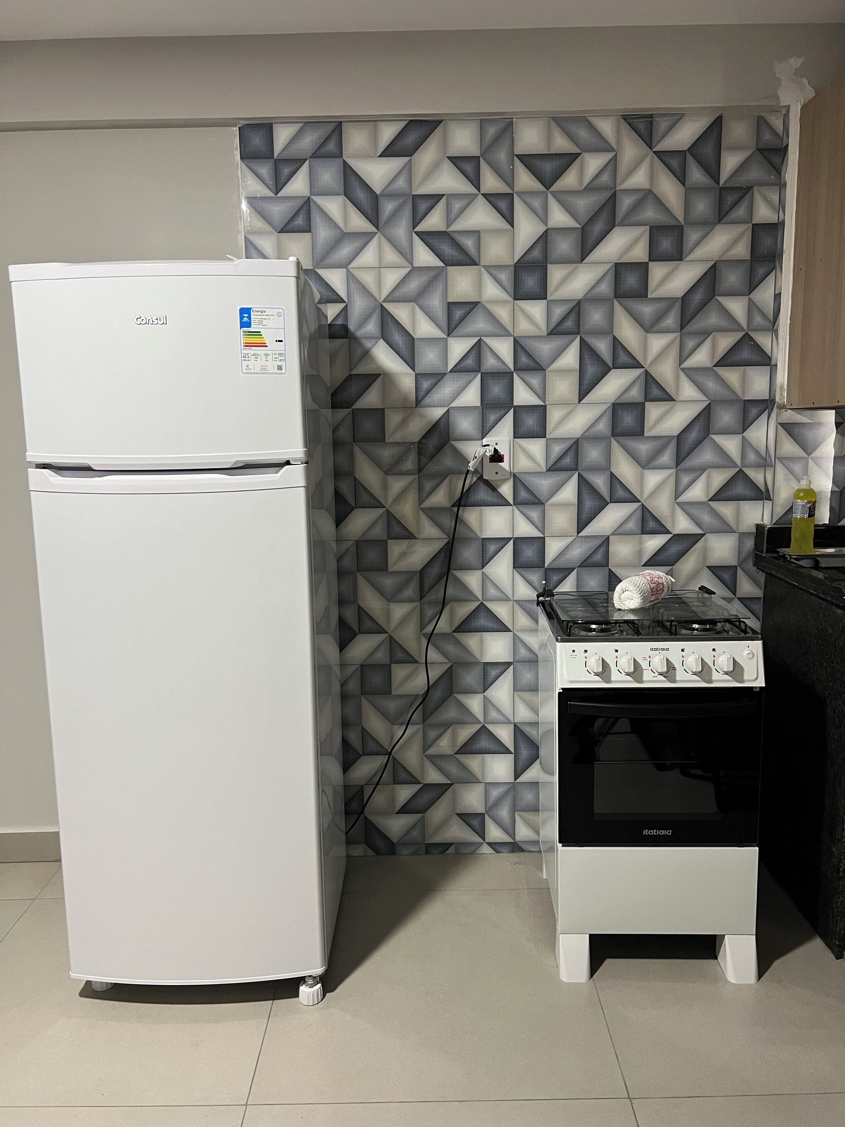 Cozinha com geladeira branca, fogão a gás e parede estampada.