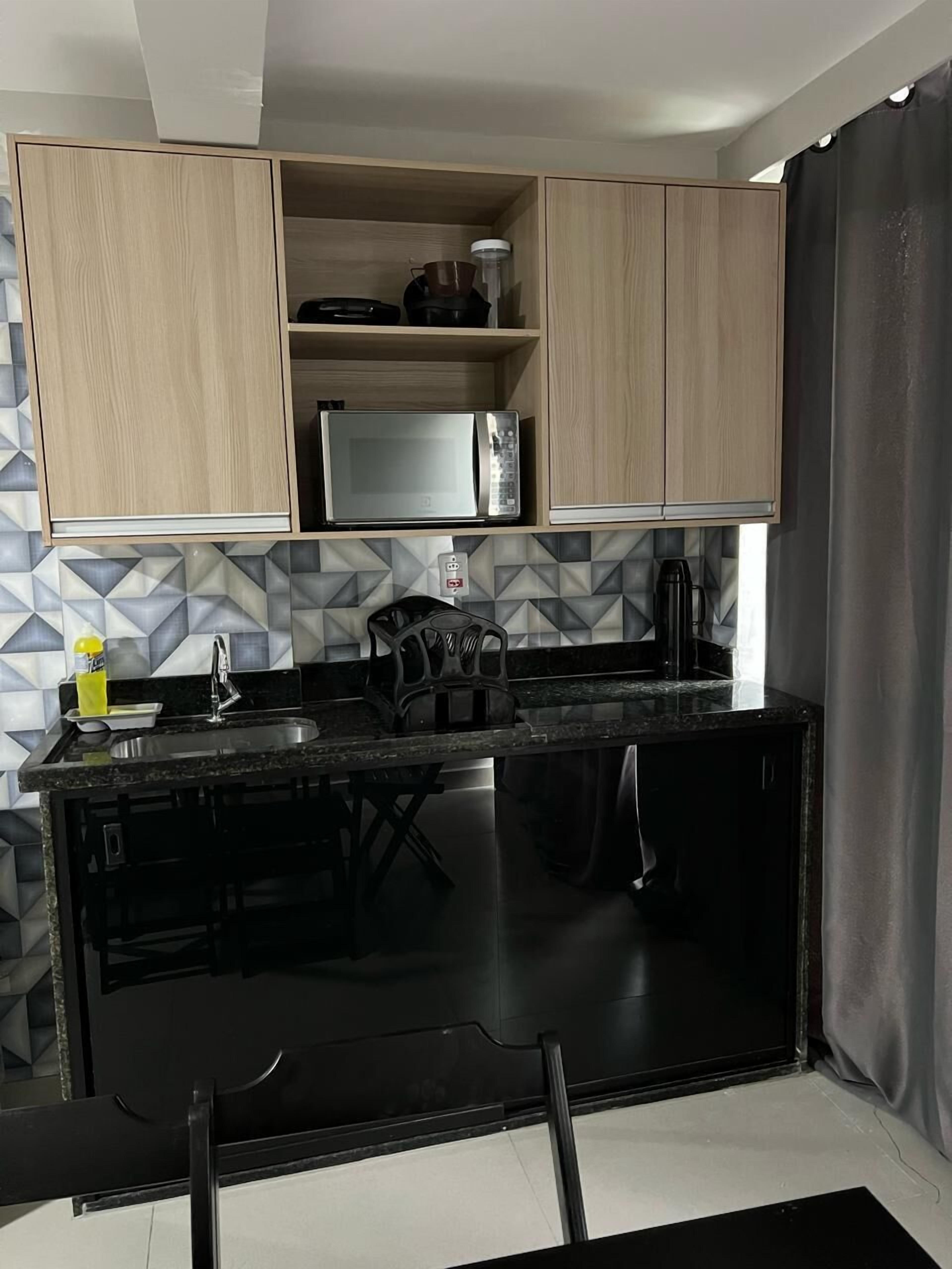 Uma cozinha compacta com micro-ondas, chaleira e cafeteira no balcão.