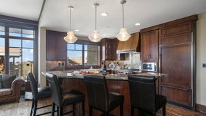 Uma cozinha moderna com armários de madeira escura, uma ilha grande com banquetas, iluminação pendente e vista para o exterior.