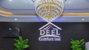 Uma área de recepção de hotel com um candelabro, uma TV de tela plana e duas plantas em vasos.