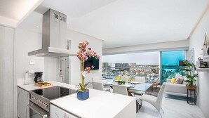 Cozinha moderna com ilha central, área de refeições com vista e sala de estar com sofá e planta.