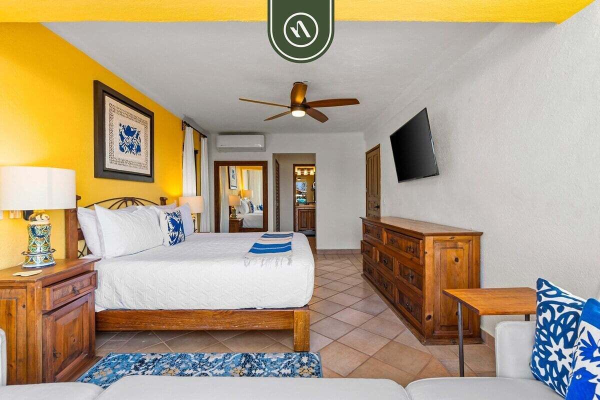 Quarto com cama, cómoda de madeira e televisão na parede.
