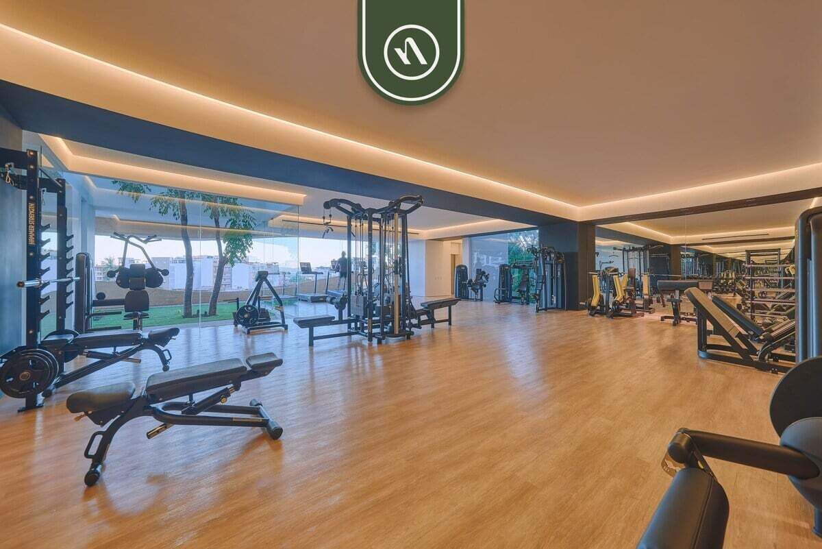 Uma academia ampla com diversos equipamentos de exercício, grandes janelas e piso de madeira.