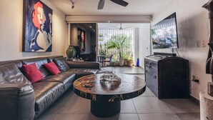 Uma sala de estar com um sofá de couro, uma mesa de centro redonda, uma televisão e uma grande pintura na parede.