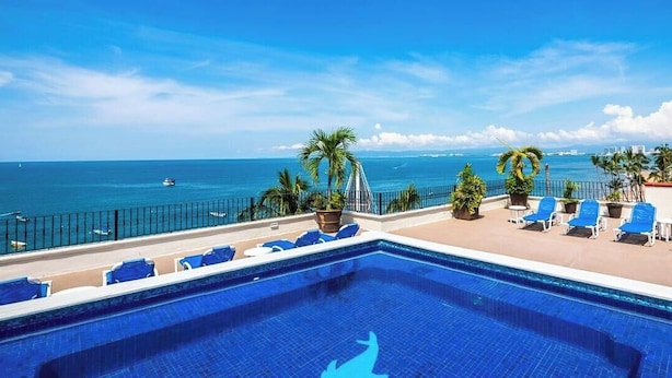 Uma piscina no terraço com vista para o oceano, cadeiras de sol e palmeiras.