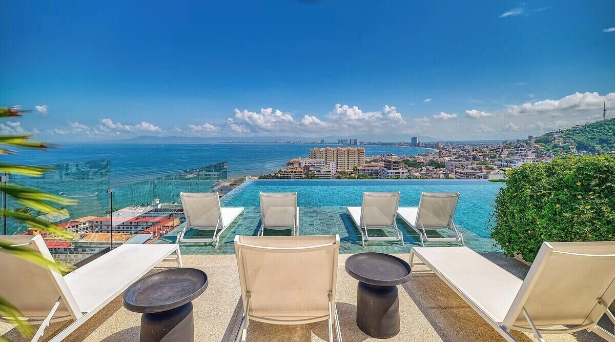 Piscina infinita com espreguiçadeiras e vista para a cidade e o oceano.