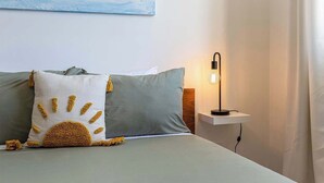 Uma cama com duas almofadas, uma luminária de cabeceira e um quadro na parede.