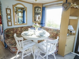 Um quarto acolhedor com uma mesa de jantar redonda posta para quatro pessoas, cercada por cadeiras confortáveis e acolchoadas. Um armário de madeira com um espelho e uma decoração em formato de coração está pendurado acima da mesa.
