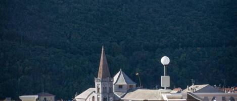 Um edifício com várias janelas pequenas, uma igreja com uma torre alta e uma montanha ao fundo.