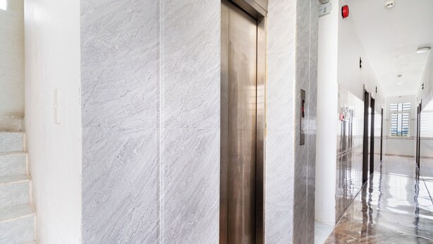 Corredor moderno com paredes de mármore e piso brilhante, que leva a um elevador.