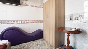Um banheiro moderno com armário de madeira, um banco acolchoado roxo e uma mesa redonda de madeira, além de um ventilador fixado na parede.