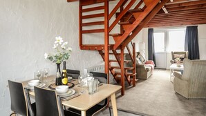 Uma sala de jantar com escada de madeira, uma mesa posta para dois e vista para a sala de estar.