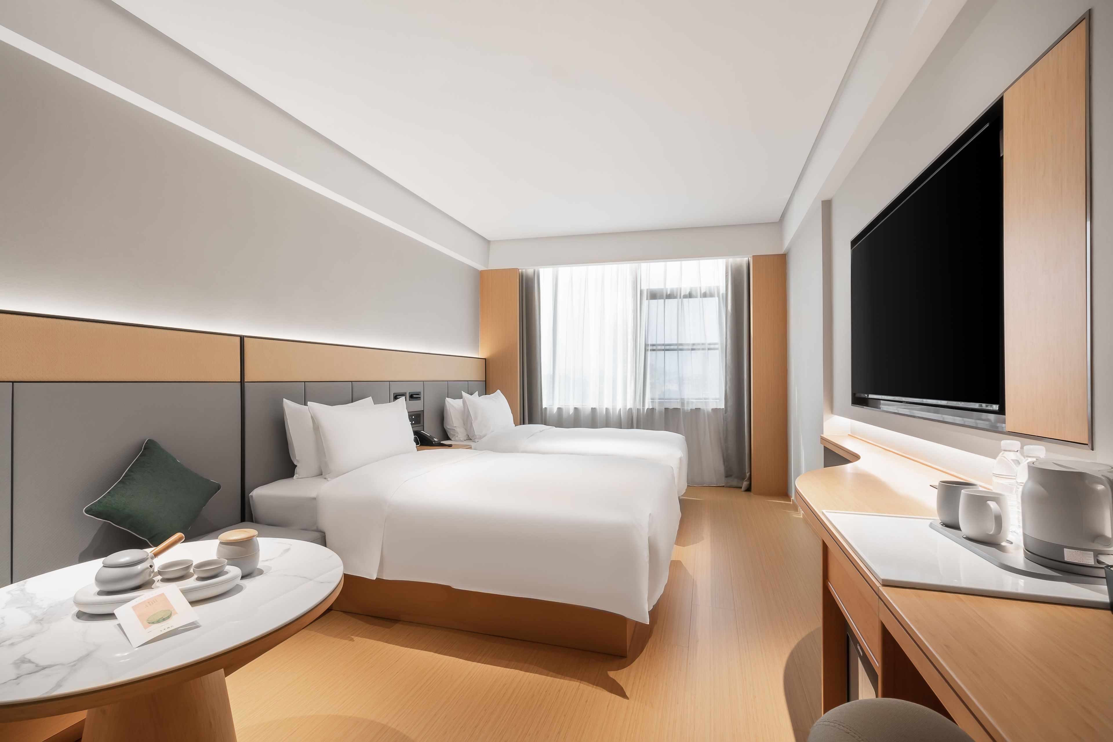 Quarto de hotel com cama, escrivaninha, televisão e janela com cortinas.