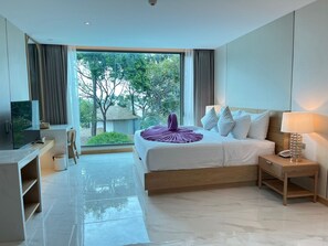 Quarto de hotel moderno com uma cama grande, uma escrivaninha, uma TV e vista para o verde lá fora.