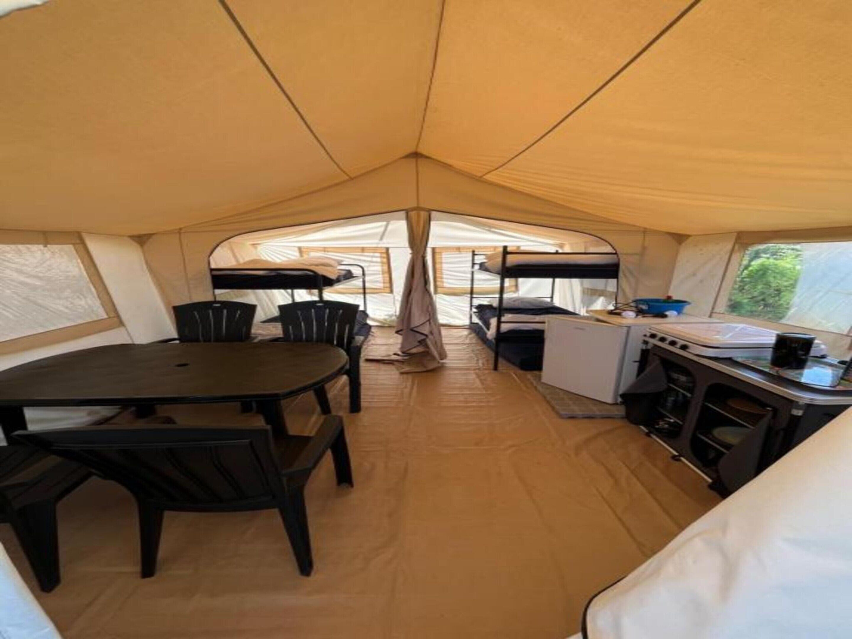 Uma tenda com mesa de jantar, cadeiras, cozinha compacta e área de dormir.