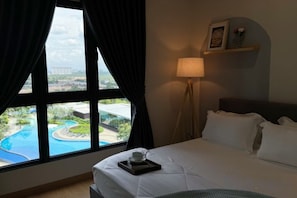 Quarto de hotel com cama, mesa de cabeceira com luminária, janela com cortinas e vista para uma piscina.
