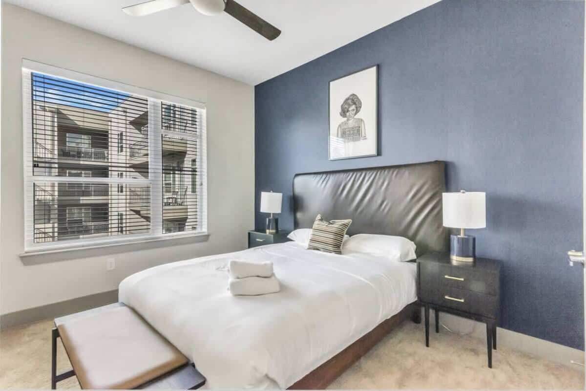Quarto moderno com uma cama grande, um ventilador de teto, uma janela com persianas e um quadro na parede.