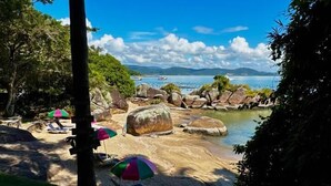 Uma praia com pedras grandes, guarda-sóis e uma vista clara do mar.