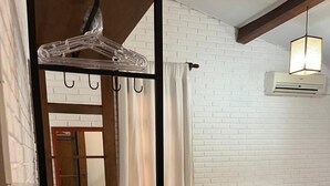 Quarto moderno com piso de madeira, um tapete cinza, uma cama branca, uma mesinha de cabeceira com abajur e uma parede de tijolos brancos.