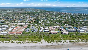 Vista aérea de uma área residencial costeira com casas, uma praia e uma ponte ao longe.