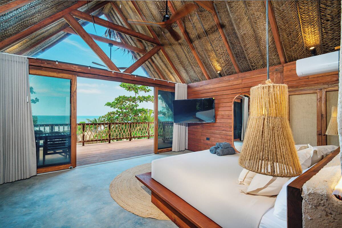 Quarto com cama grande, televisão na parede e vista para o oceano através de uma porta de correr.