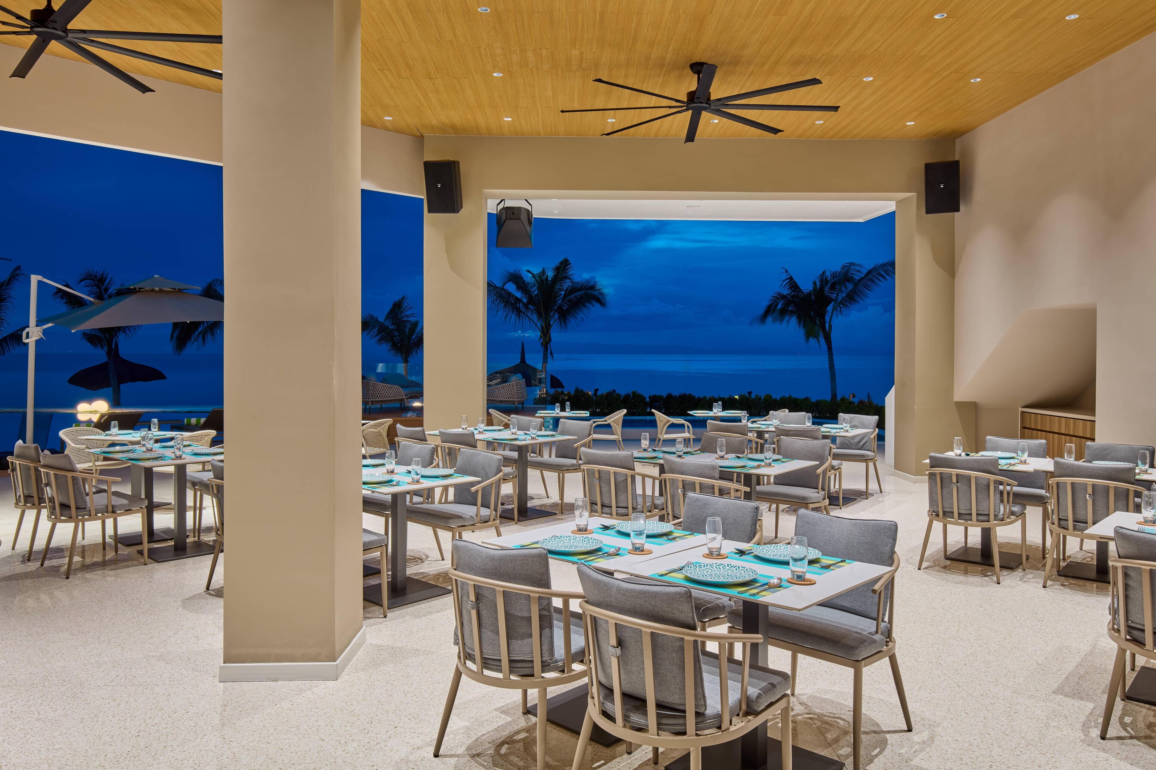 Restaurante com área externa e mesas de frente para a praia ao entardecer.