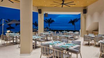 Restaurante com área externa e mesas de frente para a praia ao entardecer.