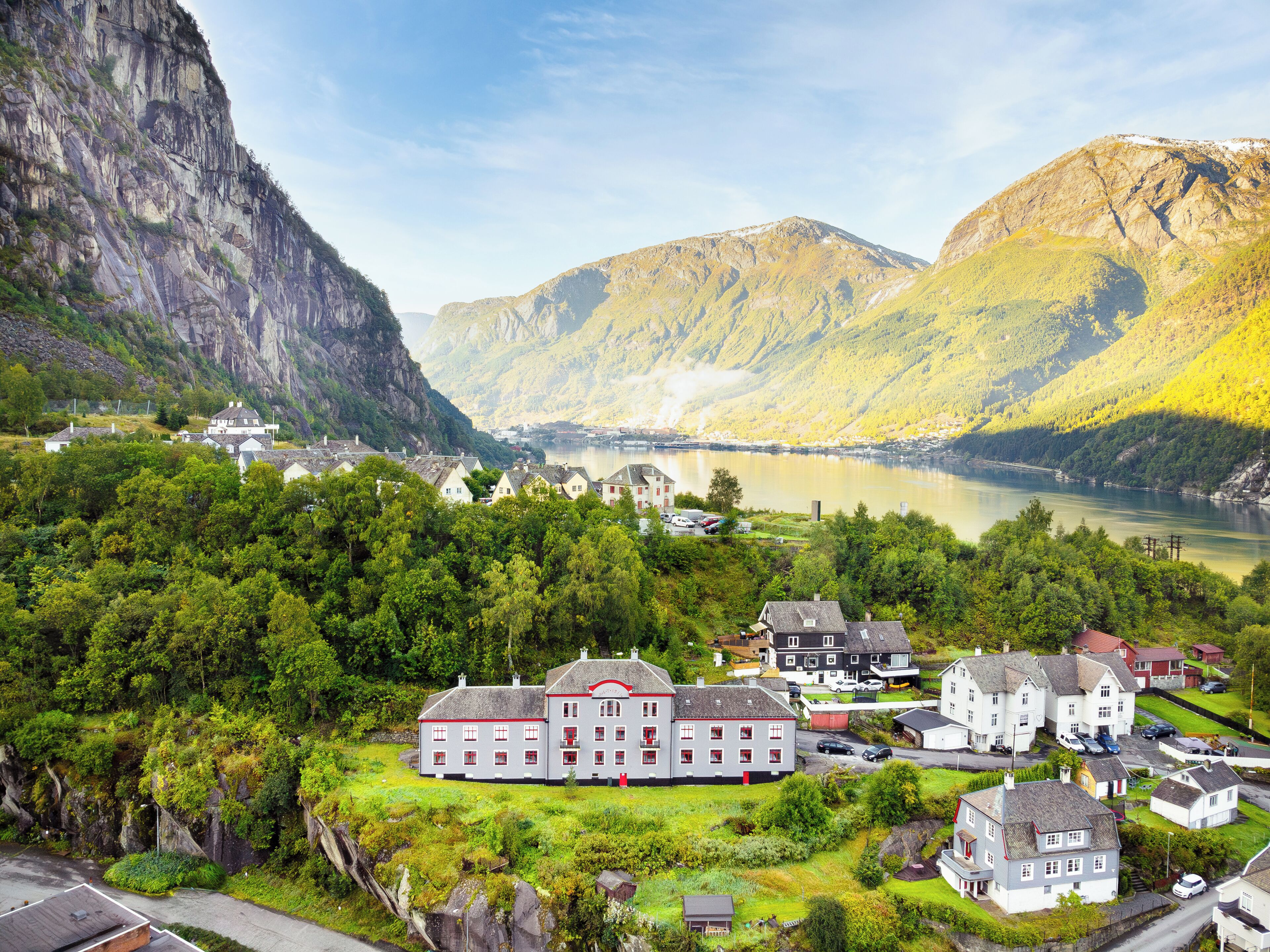 Uma vila costeira com casas tradicionais, um edifício grande com detalhes vermelhos e montanhas e um lago ao fundo.