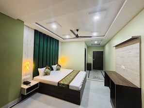 Quarto com cama, mesas de cabeceira, escrivaninha, ventoinha no teto e uma porta.
