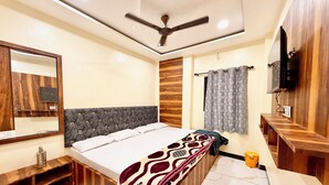 Quarto moderno com cama, cabeceira de madeira, ventilador de teto e TV fixada na parede.