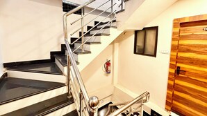 Escadaria moderna com corrimãos de metal e degraus pretos, um extintor fixado na parede e uma porta de madeira com painel de vidro.
