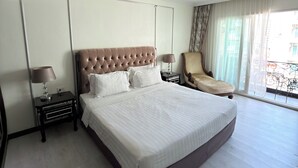 Um quarto espaçoso com uma cama grande, uma cadeira, um criado-mudo e uma janela com vista.
