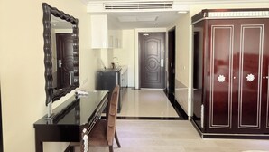 Quarto de hotel com área de refeições, um espelho grande, um guarda-roupa e uma porta que dá para outro quarto.
