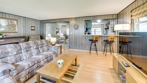 Sala de estar com sofá, mesa de centro e área de cozinha com banquetas.
