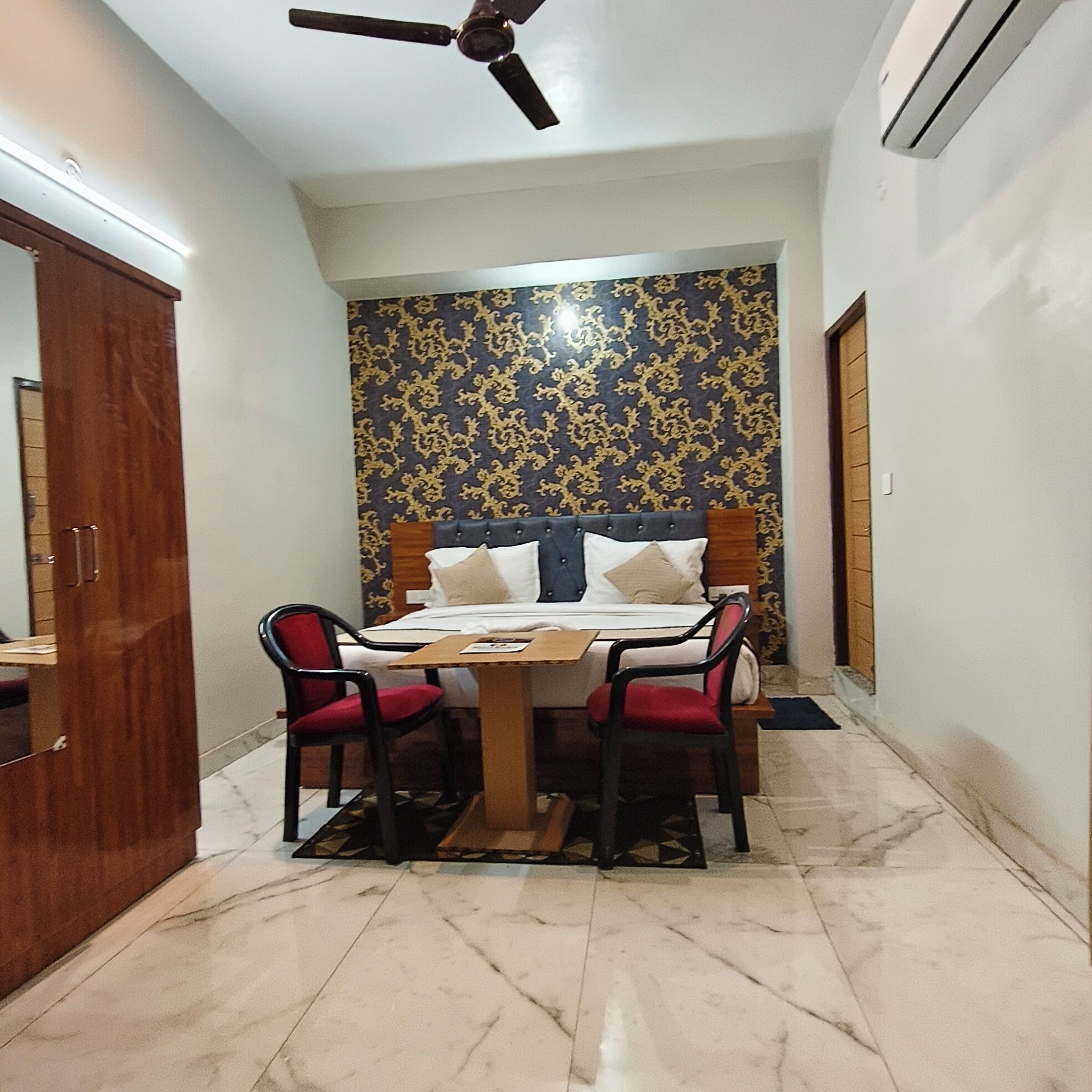 Quarto com cama, duas cadeiras, uma mesa, ventilador de teto e ar condicionado.