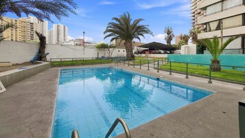 Piscina com escada de metal, rodeada por um muro baixo e palmeiras.