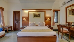 Um quarto espaçoso com uma cama grande, cabeceira de madeira, mesas de cabeceira com abajures, uma escrivaninha e uma cadeira.