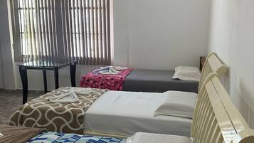 Quarto com duas camas de solteiro, uma mesinha e janela com persianas.