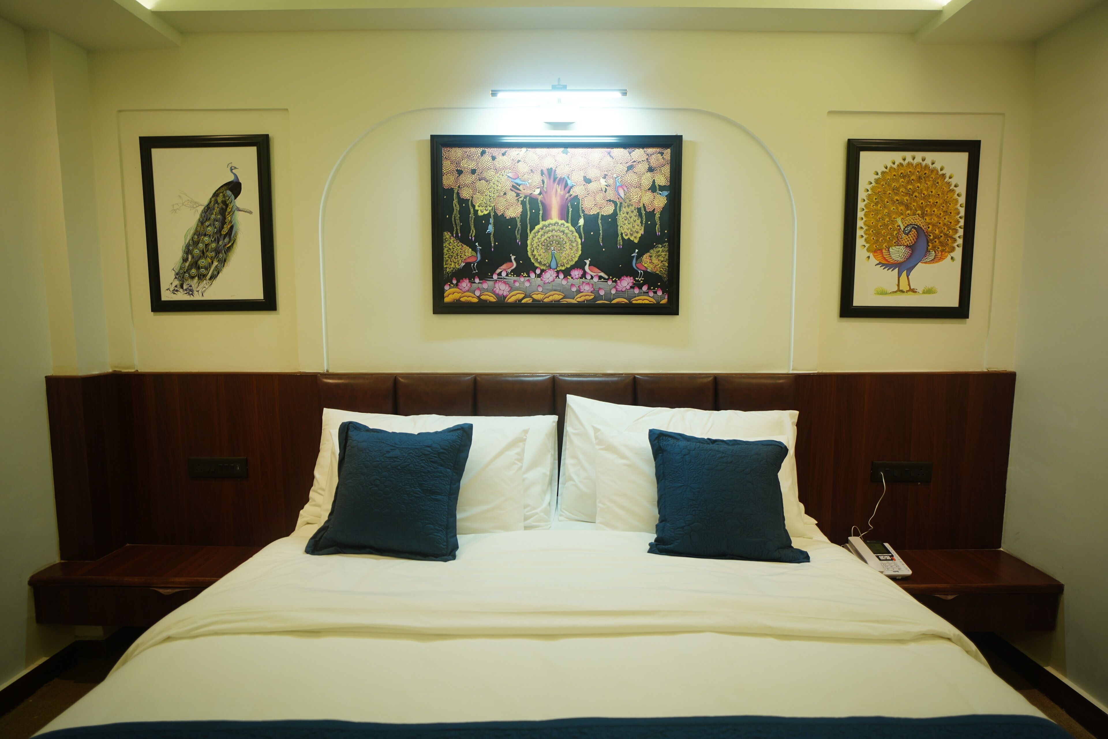 Quarto de hotel com uma cama grande, duas almofadas, uma mesa de cabeceira com um telefone e três obras de arte em molduras na parede.