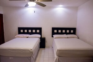 Quarto duplo com duas camas, ventoinha no teto e mesa de cabeceira.