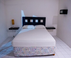 Quarto com uma cama, duas mesas de cabeceira e uma luminária fixada na parede.