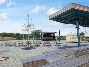 Área externa com mesas, bancos, um palco e um caminhão com a inscrição 'Dithmarscher Pilsener'.