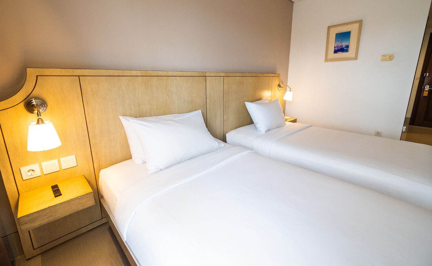 Quarto de hotel com duas camas de solteiro, cabeceiras de madeira, luminárias de cabeceira e uma pequena mesa de apoio com telefone.